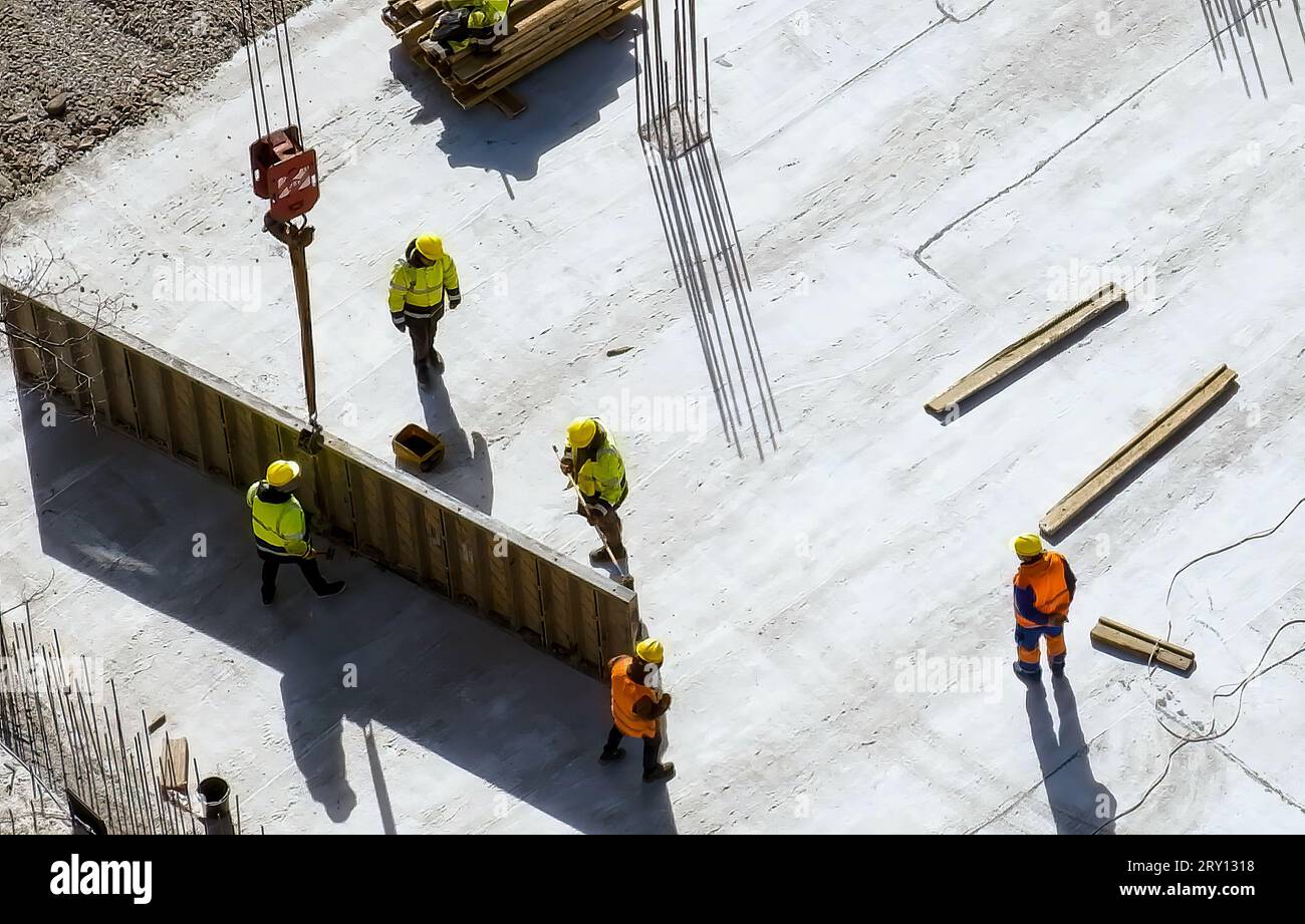 Top view: Workers in orange and yellow uniform assembling a concrete slab at the construction ...