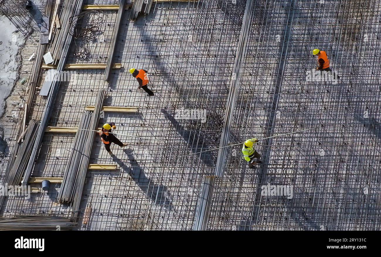 Construction Site Workers In Orange Uniform Carrying Steel Bars Rebars Floor Builders Working