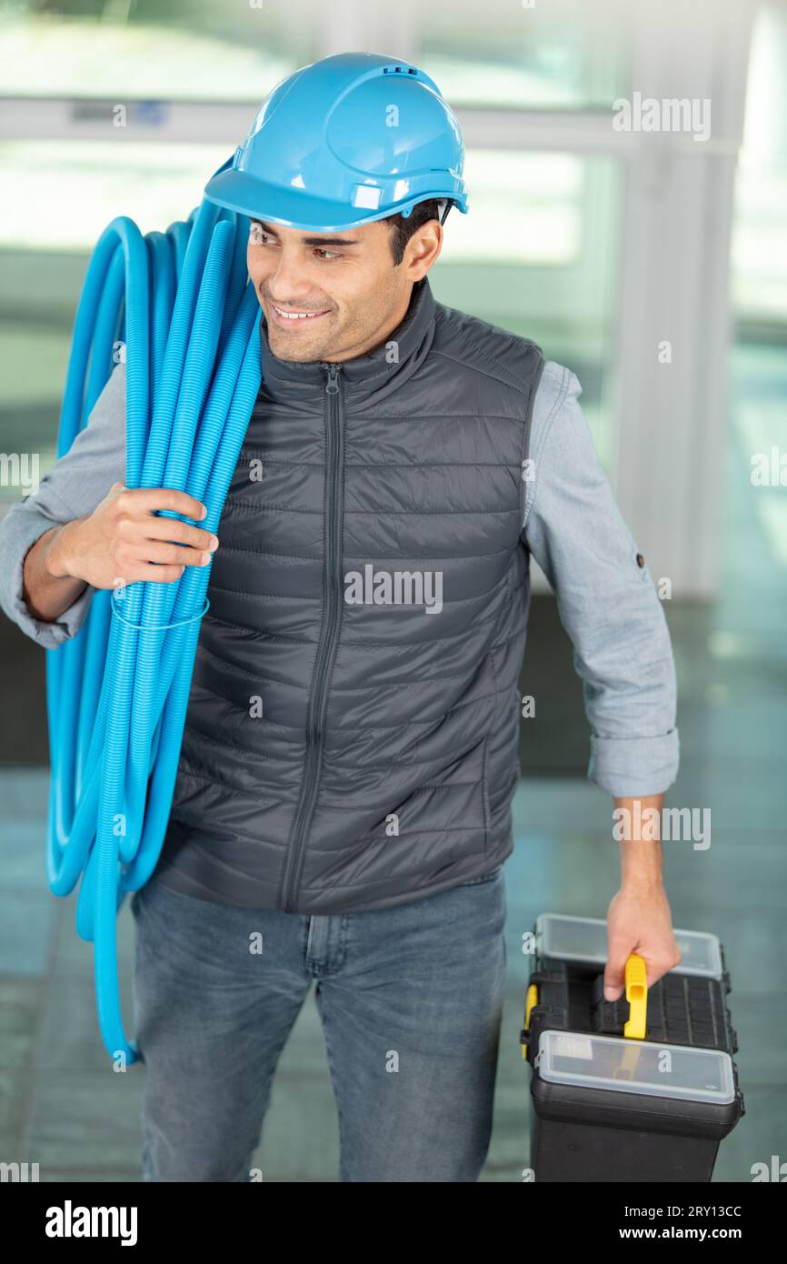 builder carrying reel of blue pipe on his shoulder Stock Photo - Alamy
