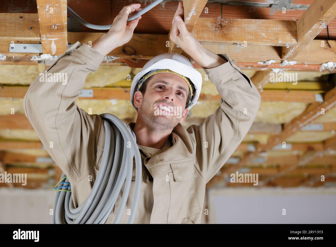 electrician installing cable trunking through wooden roof joists Stock ...