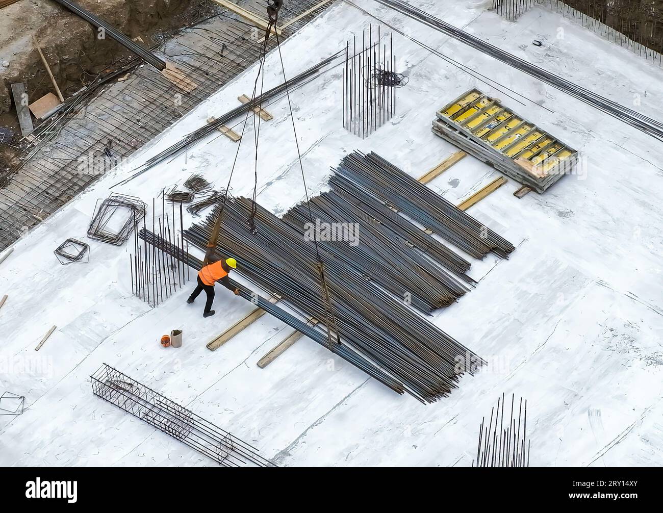 Top view: Worker in orange uniform moving steel reinforcement with a ...