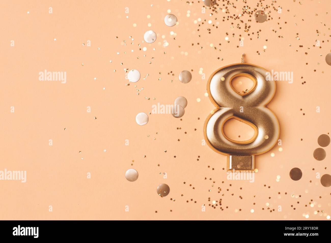 Gold candle in the form of number eight on peach background with ...