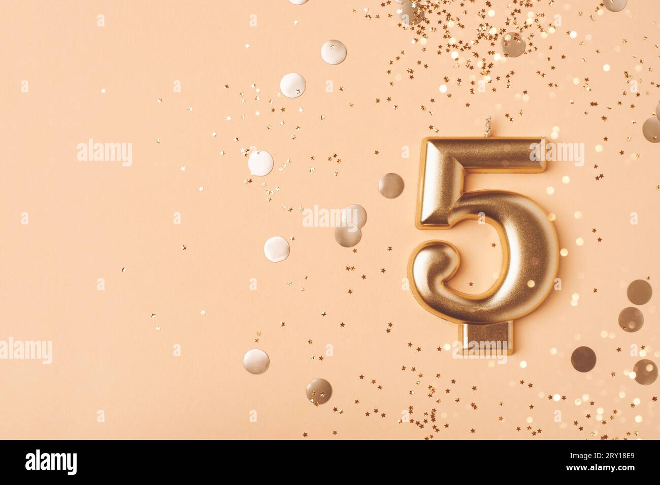 Gold candle in the form of number five on peach background with ...