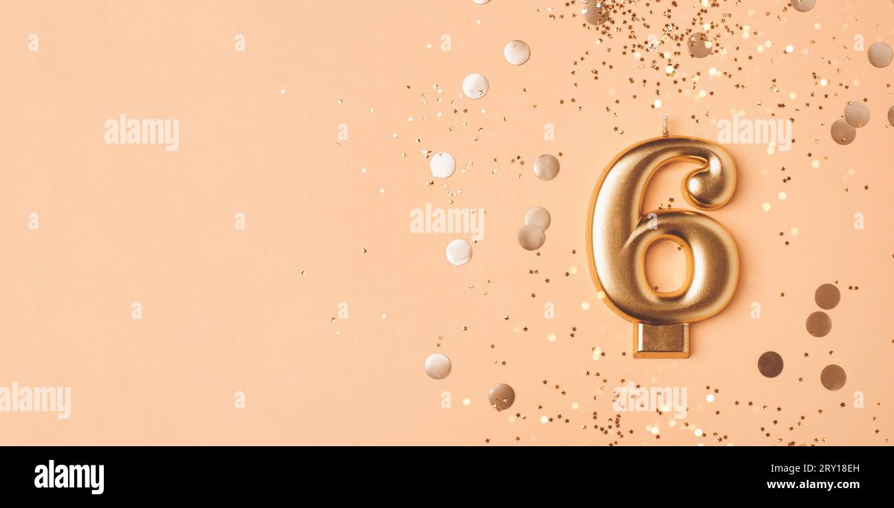 Gold candle in the form of number six on peach background with confetti ...