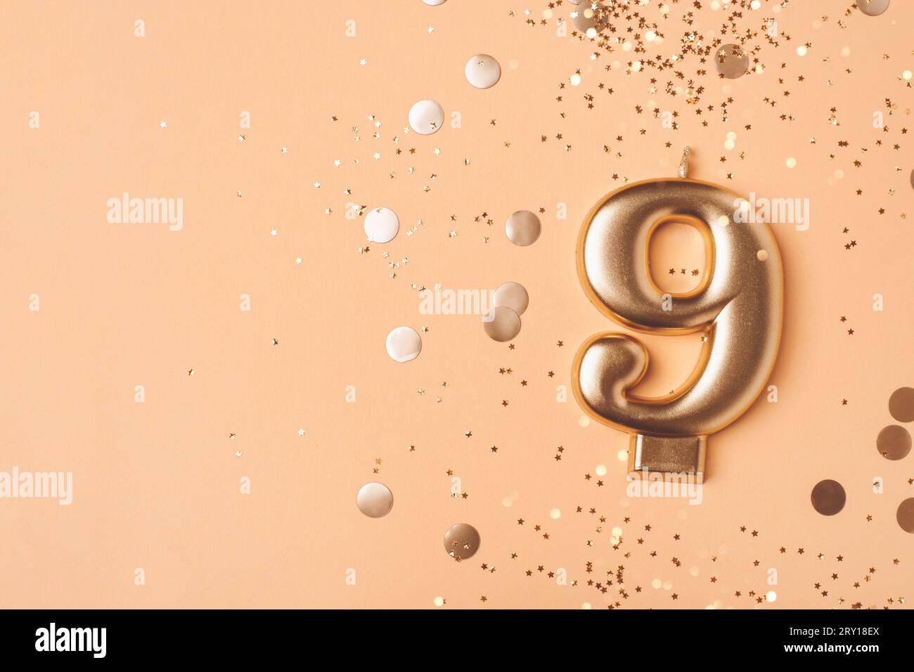 Gold candle in the form of number nine on peach background with ...