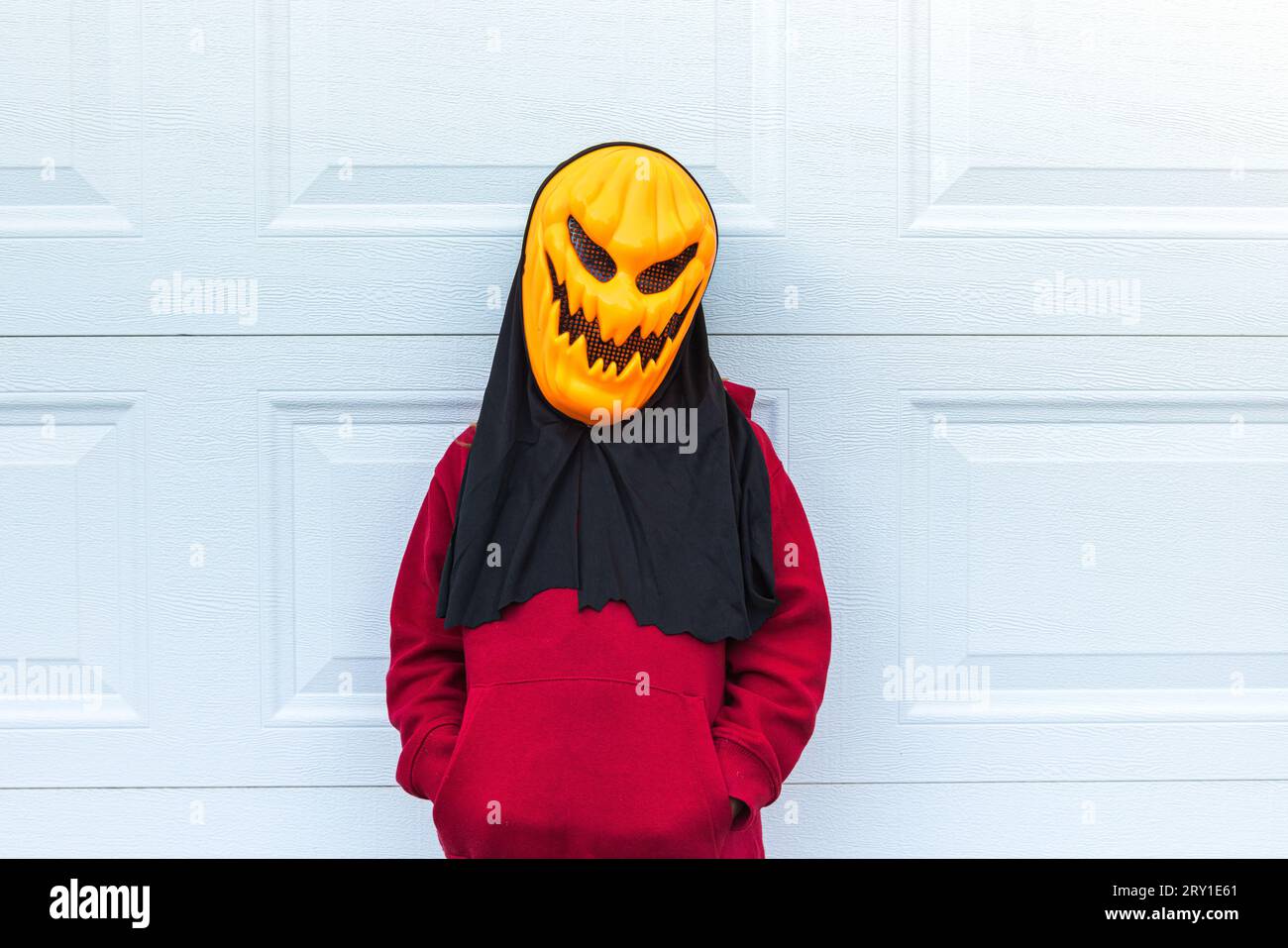 A child girl wearing a scary Halloween pumpkin mask, leaning on the ...
