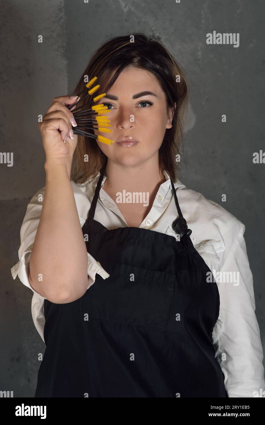 Portrait of confident young lashmaker in black apron folded yellow ...