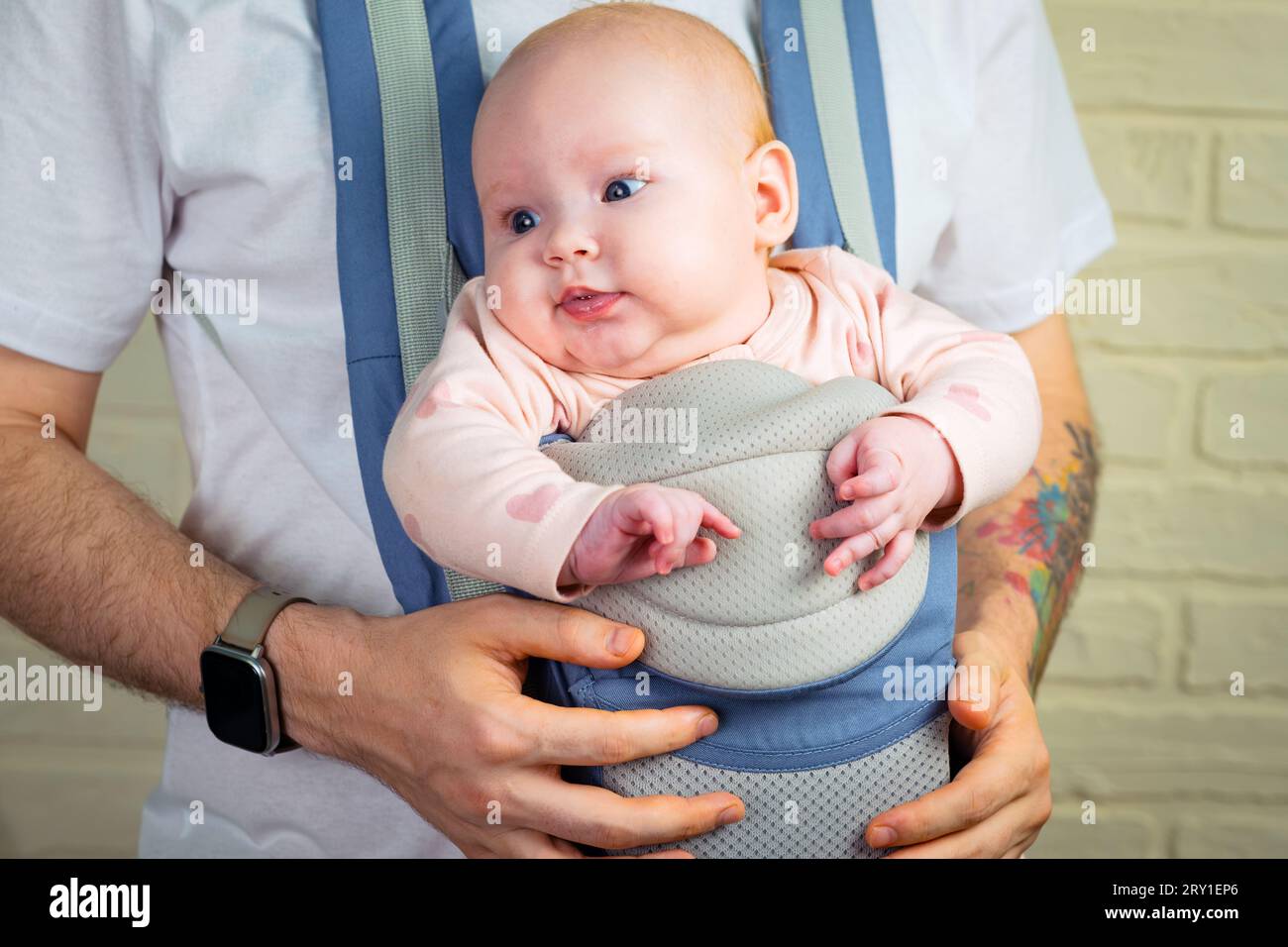 Father holding his newborn baby in a sling on a brick wall background ...