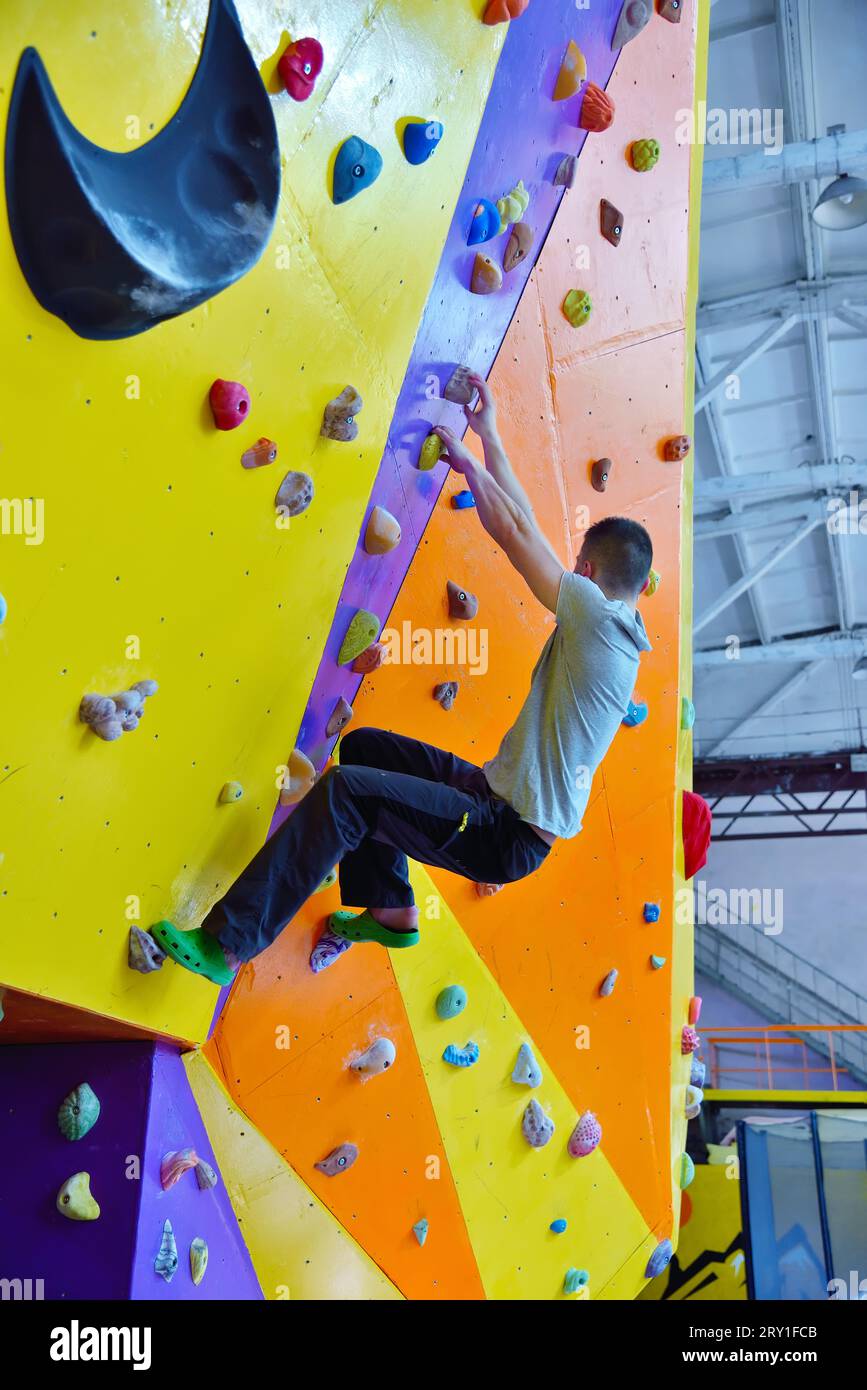 Young man climbing up on practice wall in gym. Extreme and healthy ...