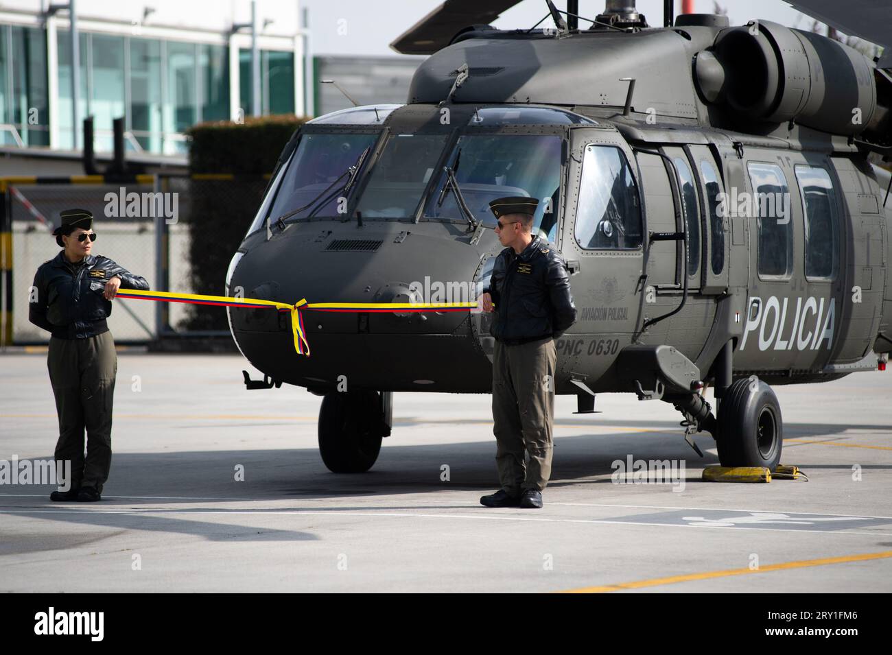 Two pilots hold a ribbon of the Colombian flag in front of a UH60 Black ...