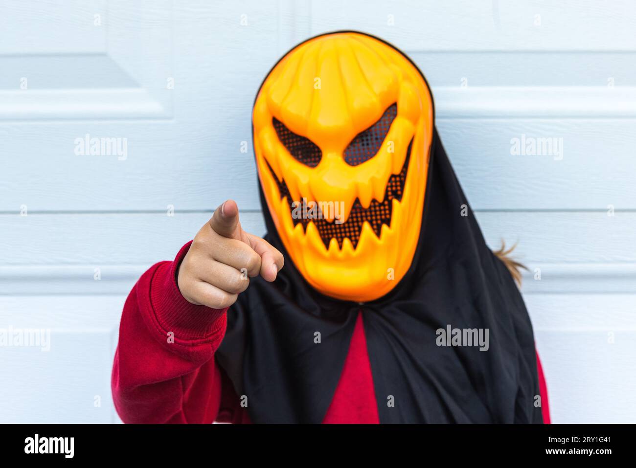 A child girl wearing a scary Halloween pumpkin mask, pointing a finger ...