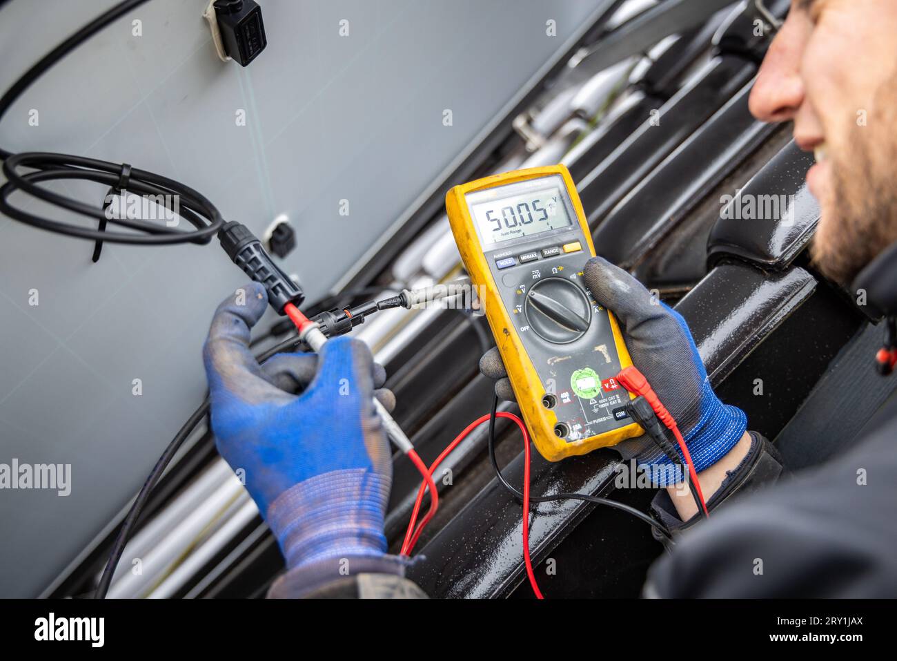 Technician with a multimeter testing a solar panel on a roof for its ...