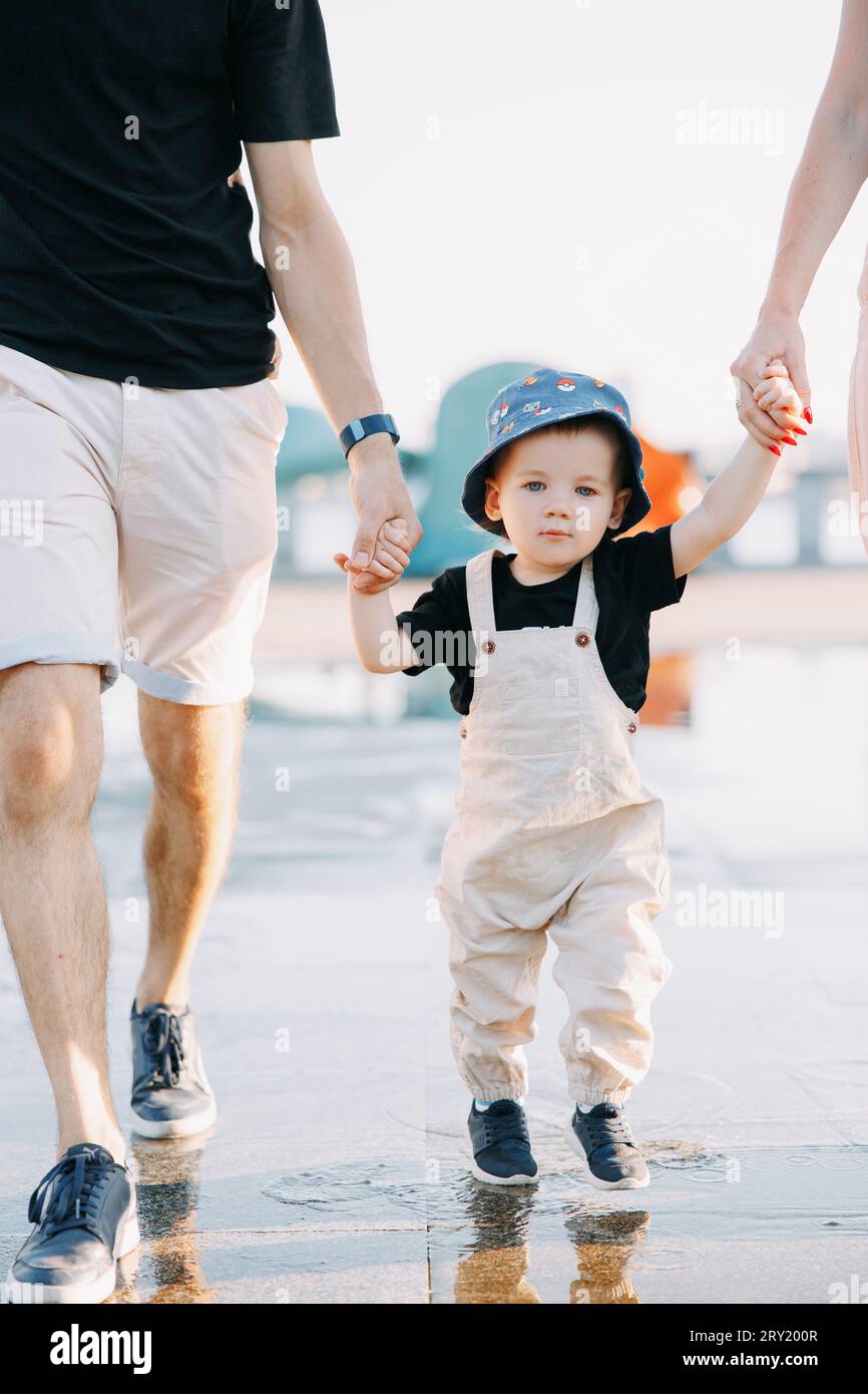 Close-up view to toddler boy holding for hands of his parents during ...