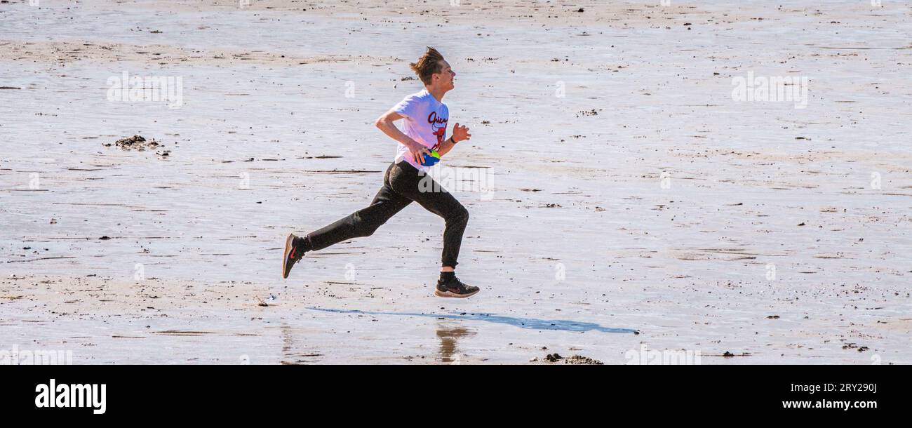 A panoramic image of a male teenager running along Fistral Beach in ...