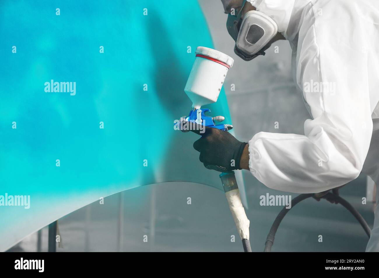Professional spray painter in protective mask and clothes spraying car ...