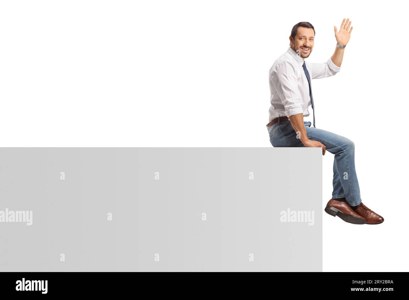 Young professional man sitting on a white wall and waving isolated on ...
