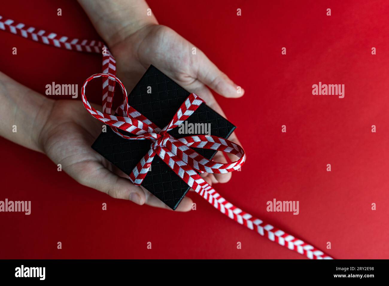 Crop anonymous person with small present box in daytime holiday on red ...
