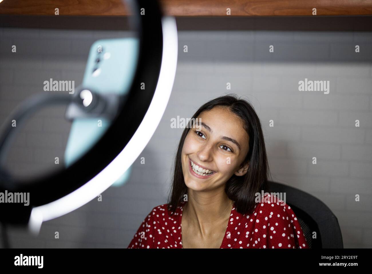 Positive young female vlogger in dress sitting in front of tripod with ...