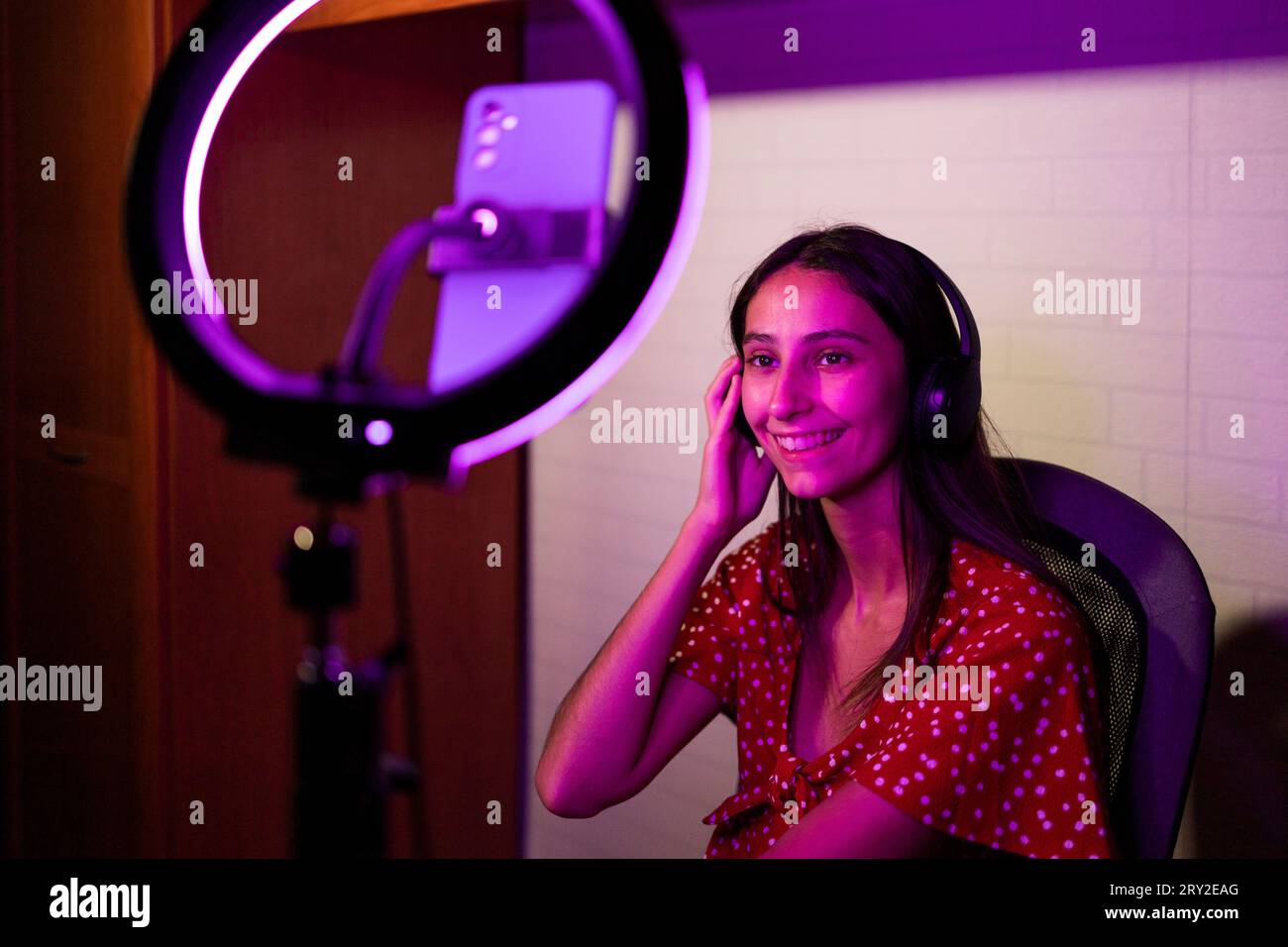 Positive young female vlogger in dress and headphones sitting in front ...