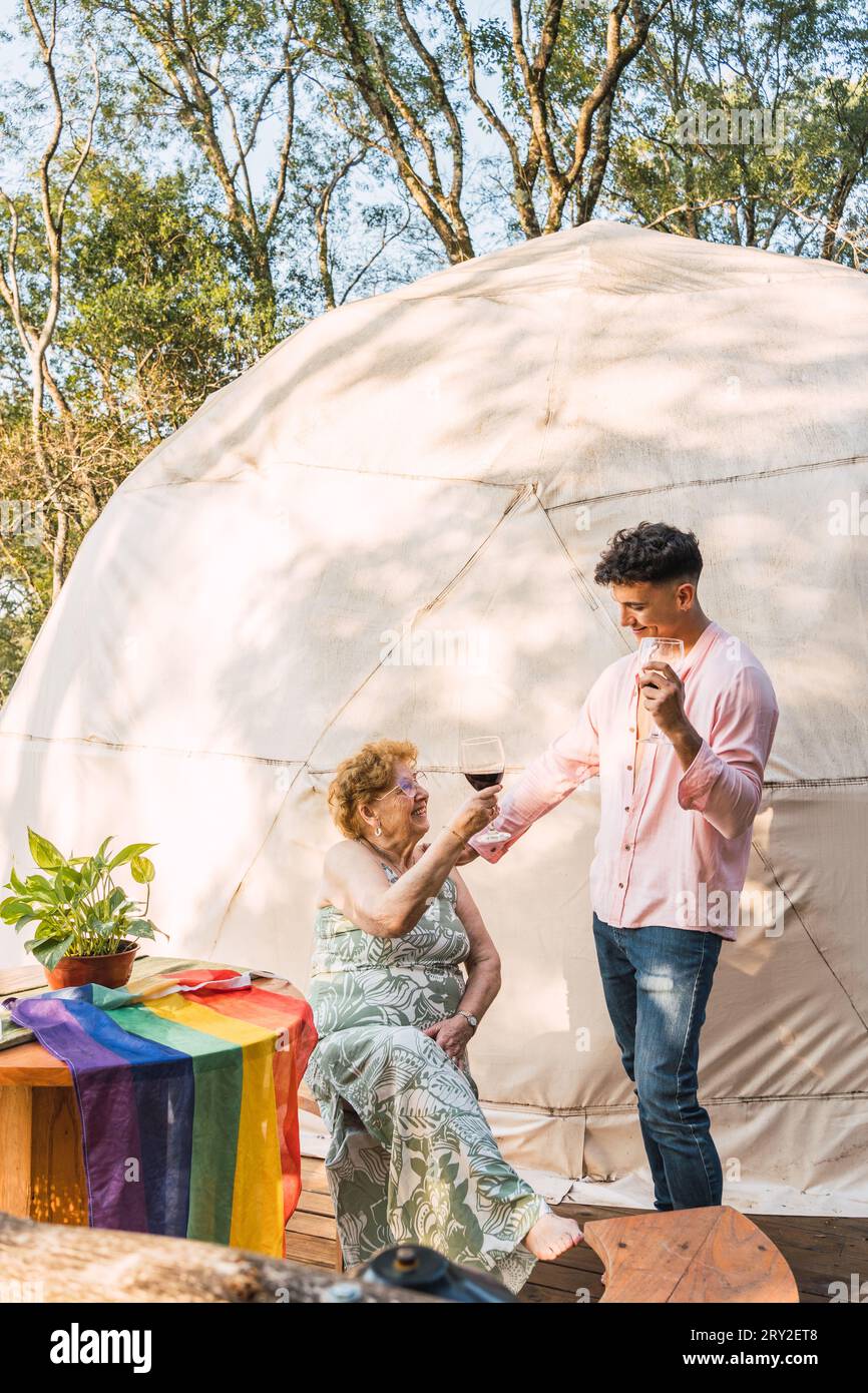 Full body of senior female toasting wineglass to LGBT son while sitting ...
