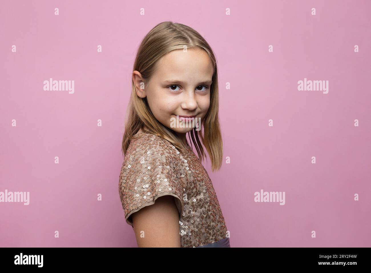 Pretty little child girl with cute smile posing over pink studio wall ...