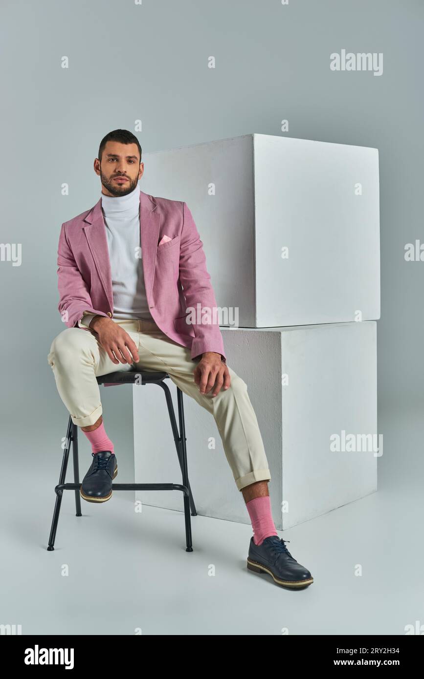elegant man in business attire sitting on chair and looking at camera ...