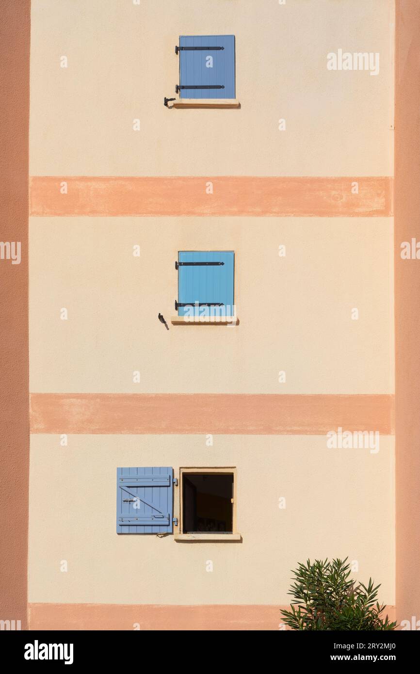 Two closed and one open blue shuttered windows on a wall in Le Barcares ...