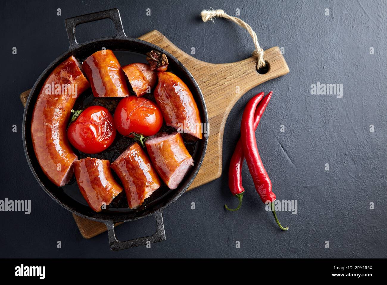 Fatty pork sausage fried with whole tomatoes in a cast iron frying pan ...