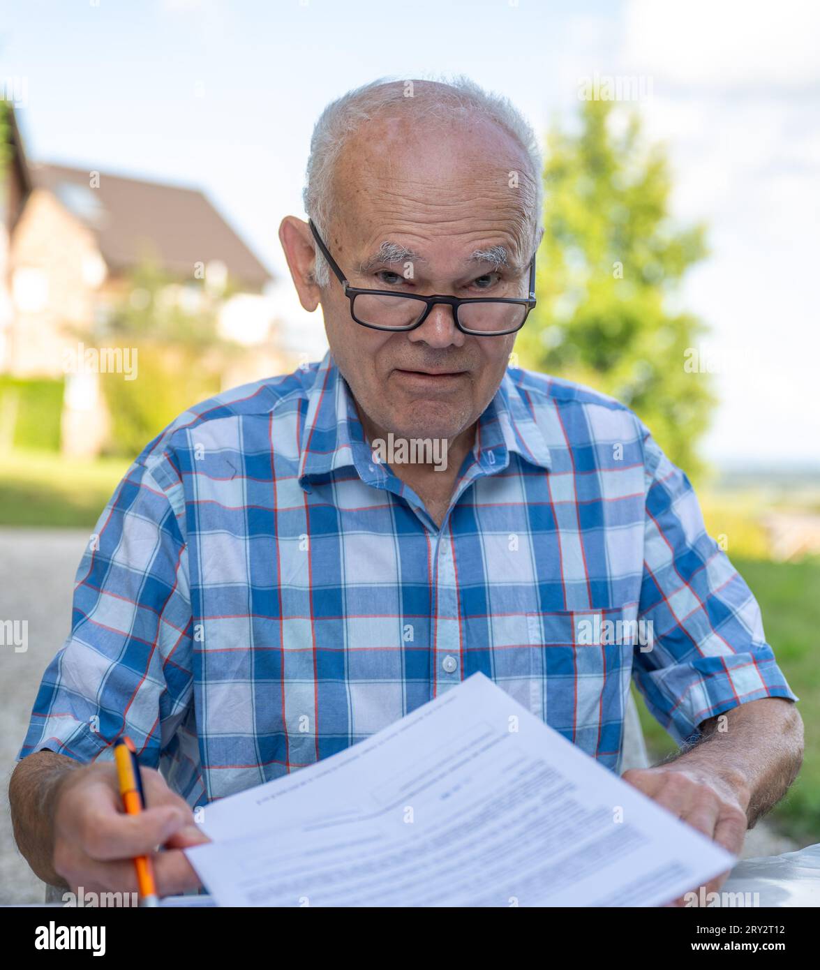 An elderly man sits at a desk outside, working with documents, filling ...
