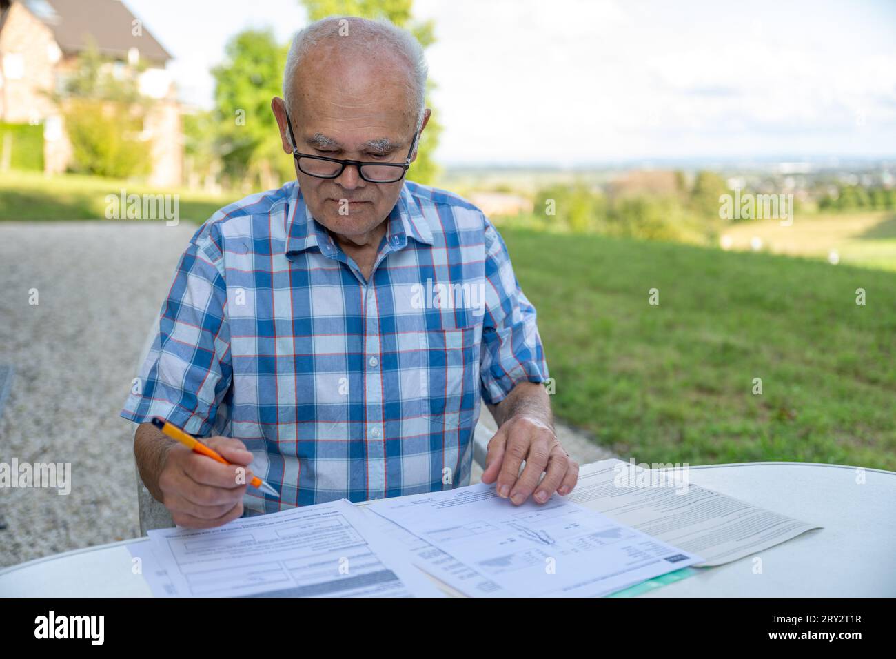An elderly man sits at a desk outside, working with documents, filling ...