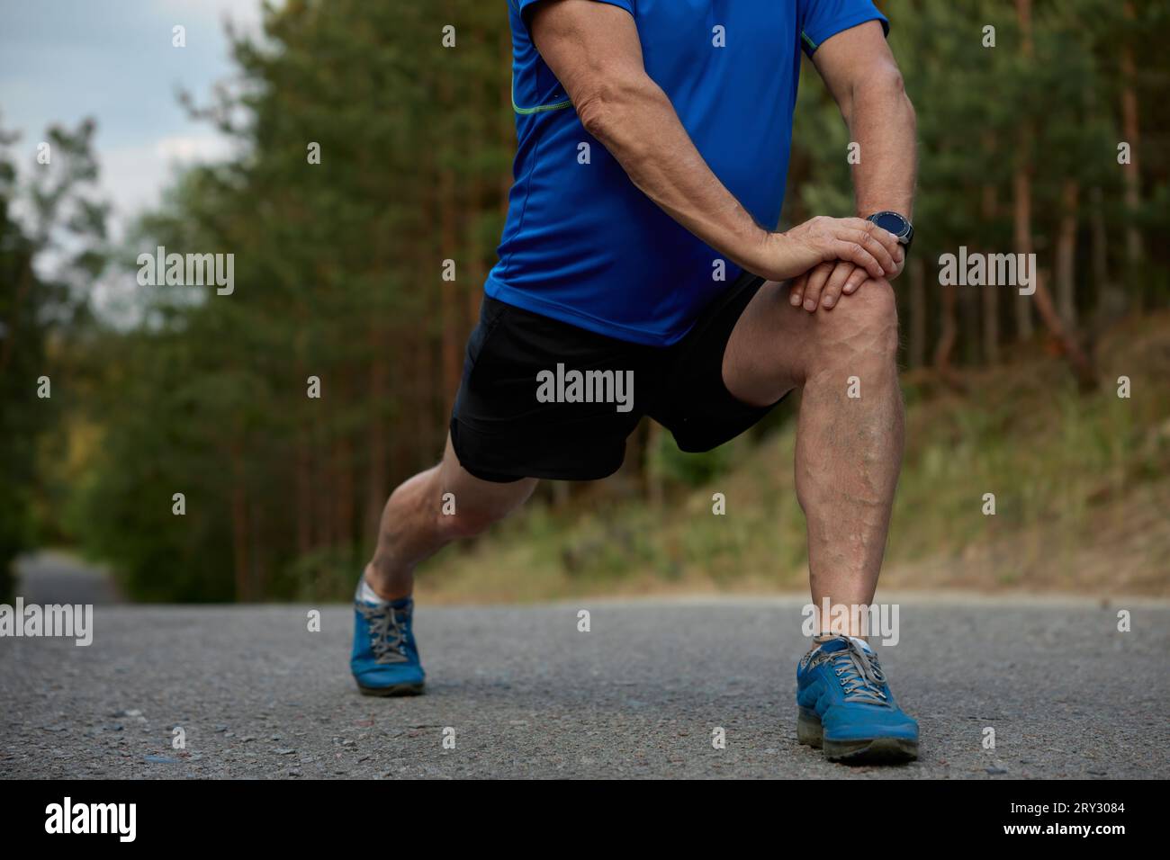 Crop view of mature athlete warming up muscles before running practice ...