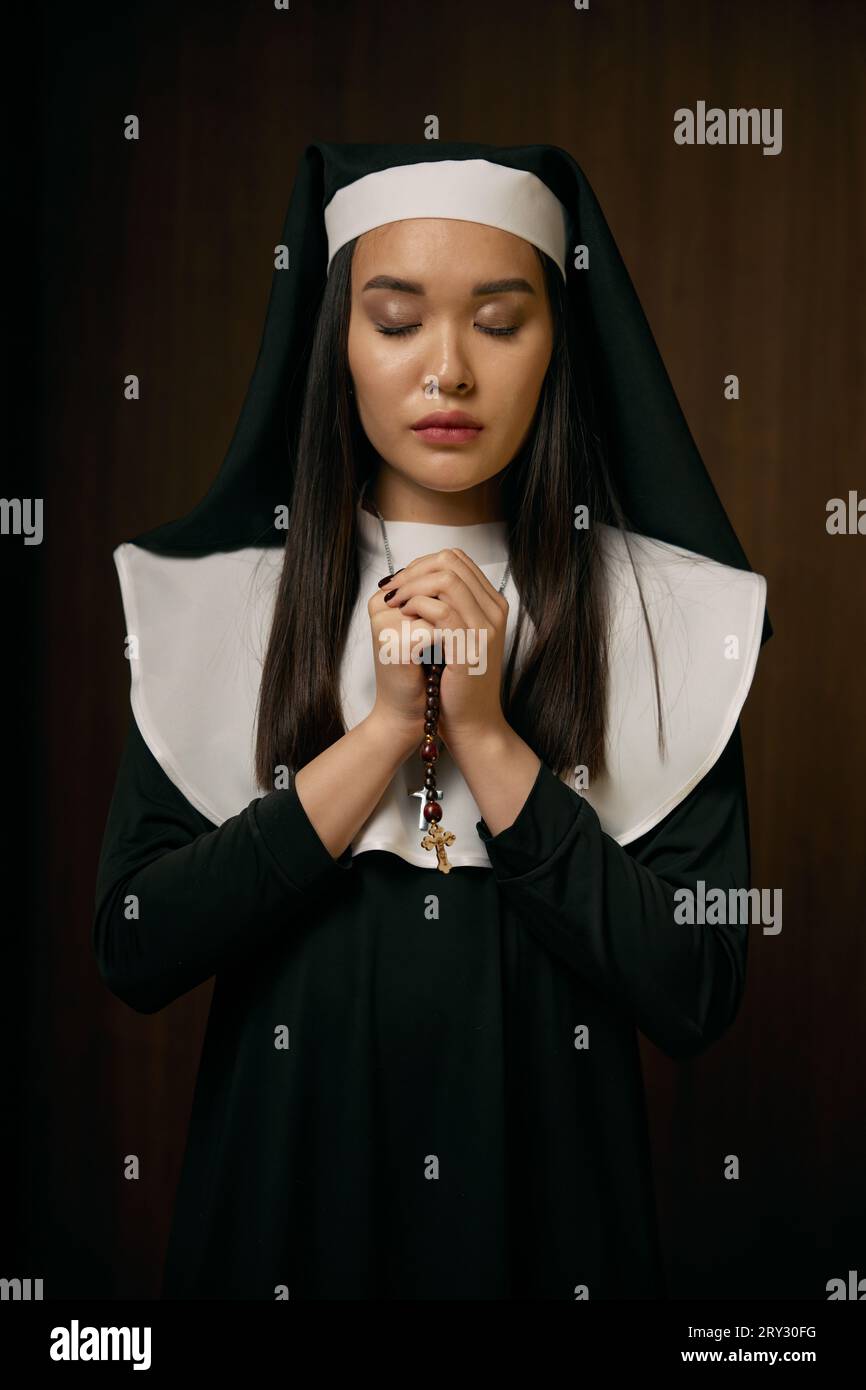 Portrait of religious nun praying with eyes closed holding crucifix ...