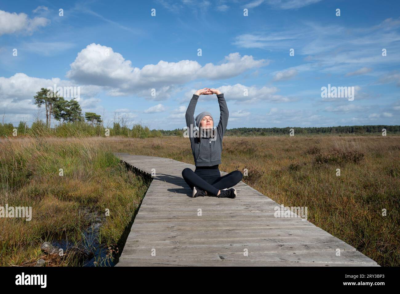 Sporty woman sitting cross legged doing an arm stretch warm up exercise ...