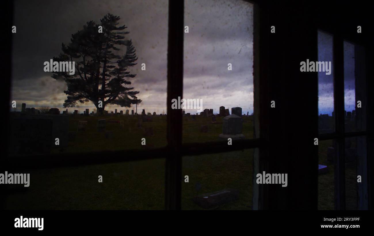View through an old antique window of a gloomy graveyard cemetery and a ...