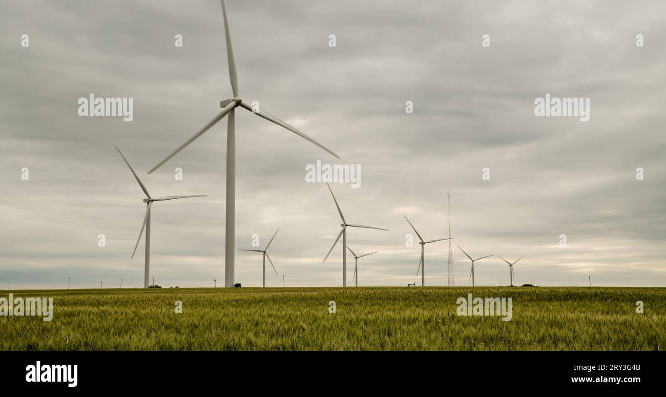 Dreamy vision of wind turbines that tower above a green wheat field and ...