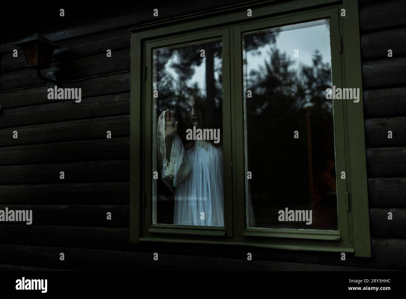 Female ghost looking through glass window of haunted cabin Stock Photo ...