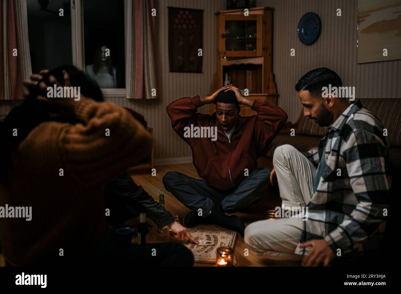 Shocked friends looking at woman touching ouija board while ghost at ...