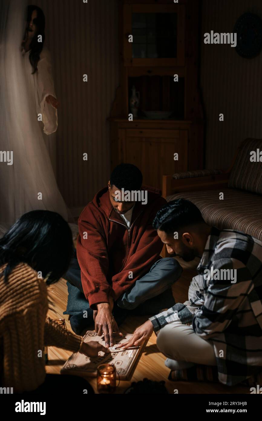 Ghost with hand reaching towards men and woman touching ouija board in ...