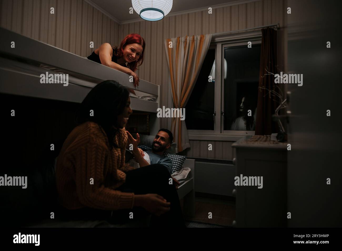 Multiracial friends having fun in cabin while ghost looking through ...