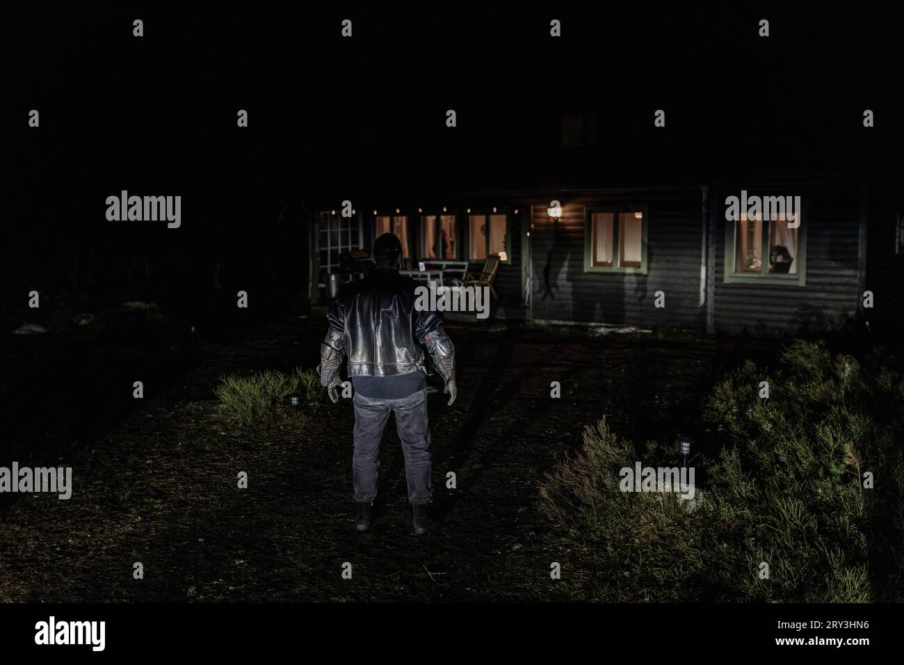 Rear view of demon standing in front of illuminated cabin at night ...