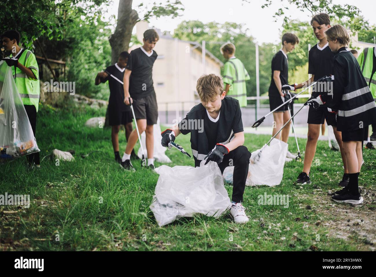 Boy kneeling while collecting garbage in plastic bag near friends Stock ...