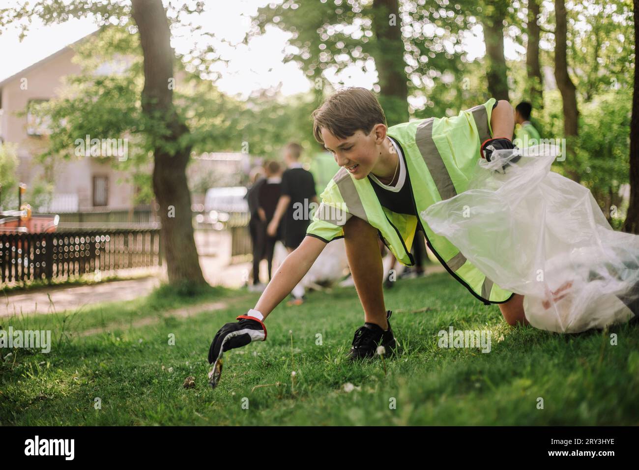 Smiling teenage boy collecting plastic in garbage bag Stock Photo - Alamy