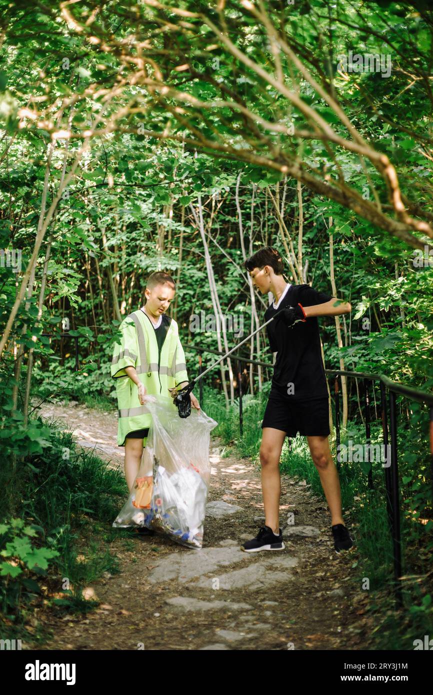 Full length of boys collecting garbage on bag amidst plants Stock Photo ...