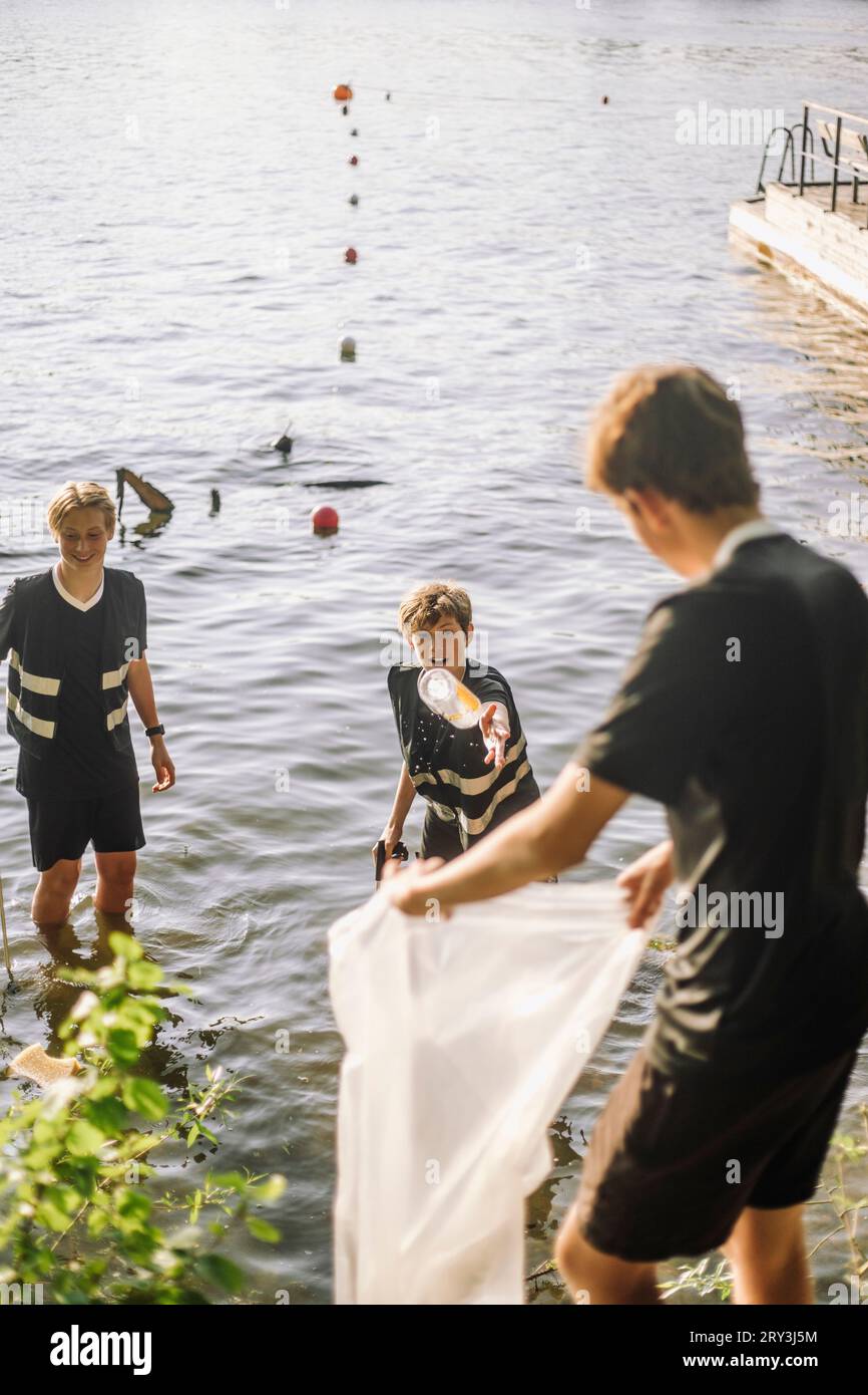Boy throwing plastic bottle in bag held by friend Stock Photo - Alamy