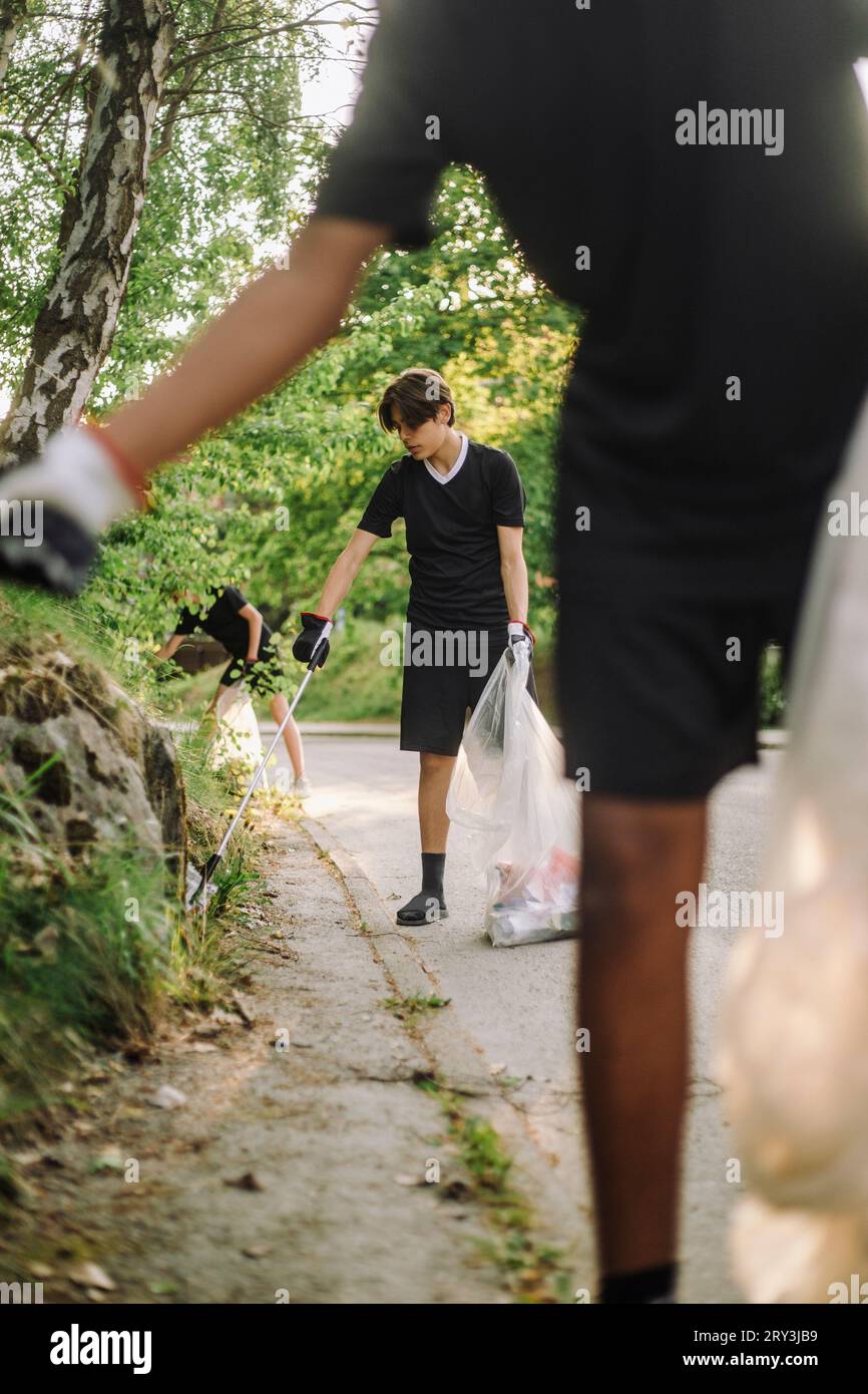 Teenage boys collecting plastic from plants in garbage bags on road ...