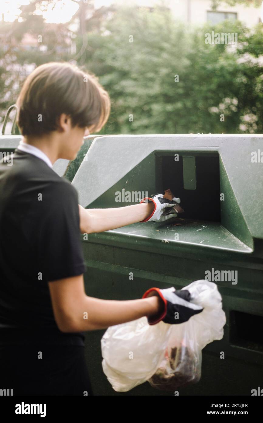 Teenage boy putting plastic garbage in recycling bin Stock Photo - Alamy