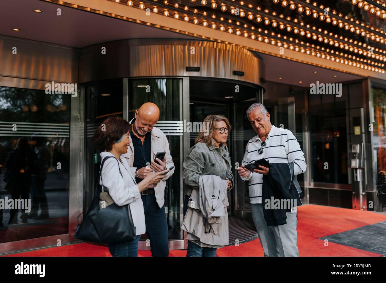 Male and female senior friends sharing smart phones while standing ...
