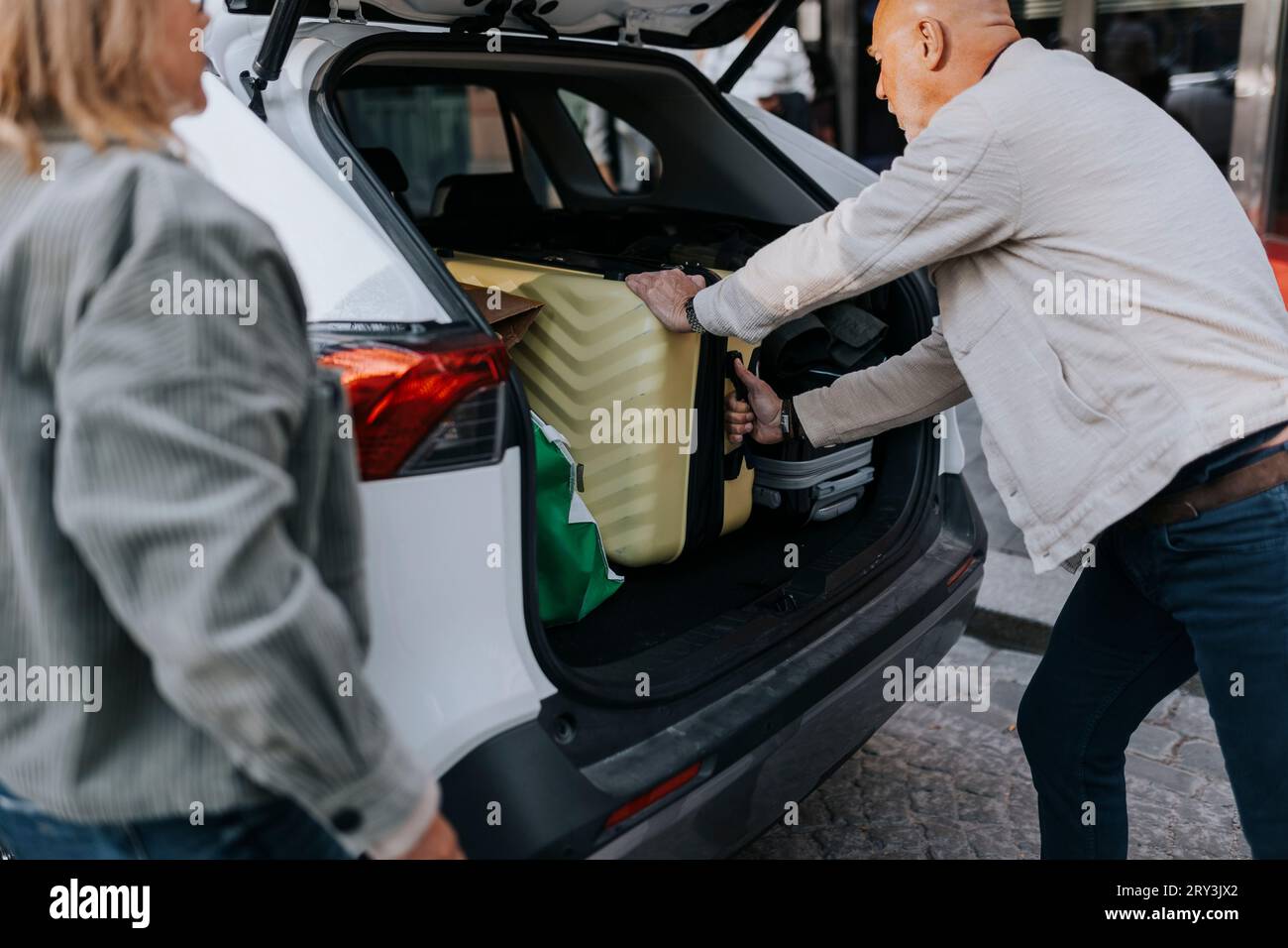 Side view of elderly man loading suitcase in car trunk Stock Photo - Alamy