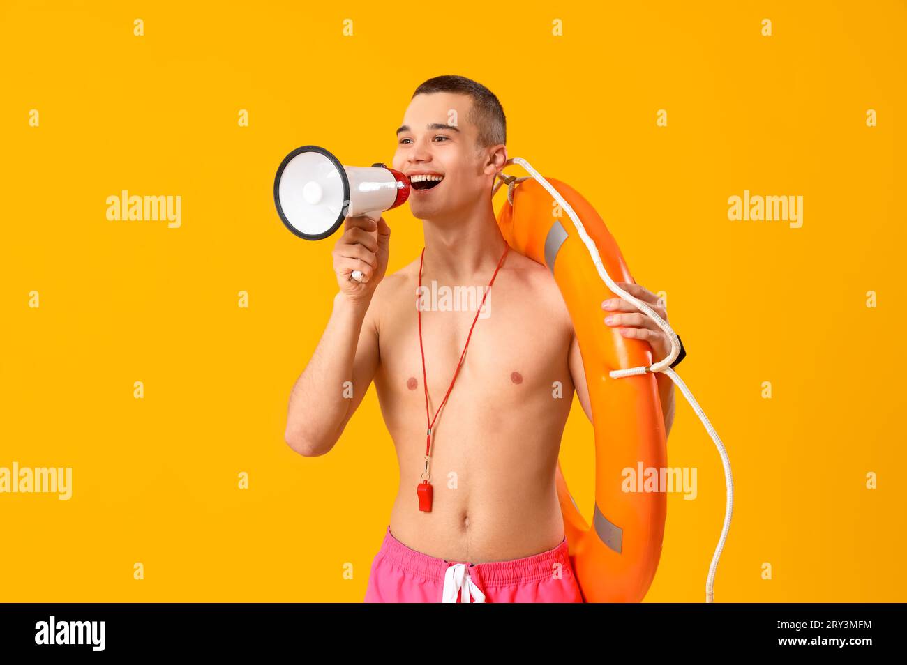 Male lifeguard with ring buoy shouting into megaphone on yellow ...