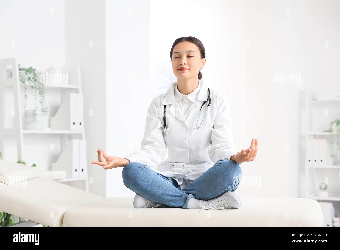 Female Asian doctor meditating on couch in clinic Stock Photo - Alamy